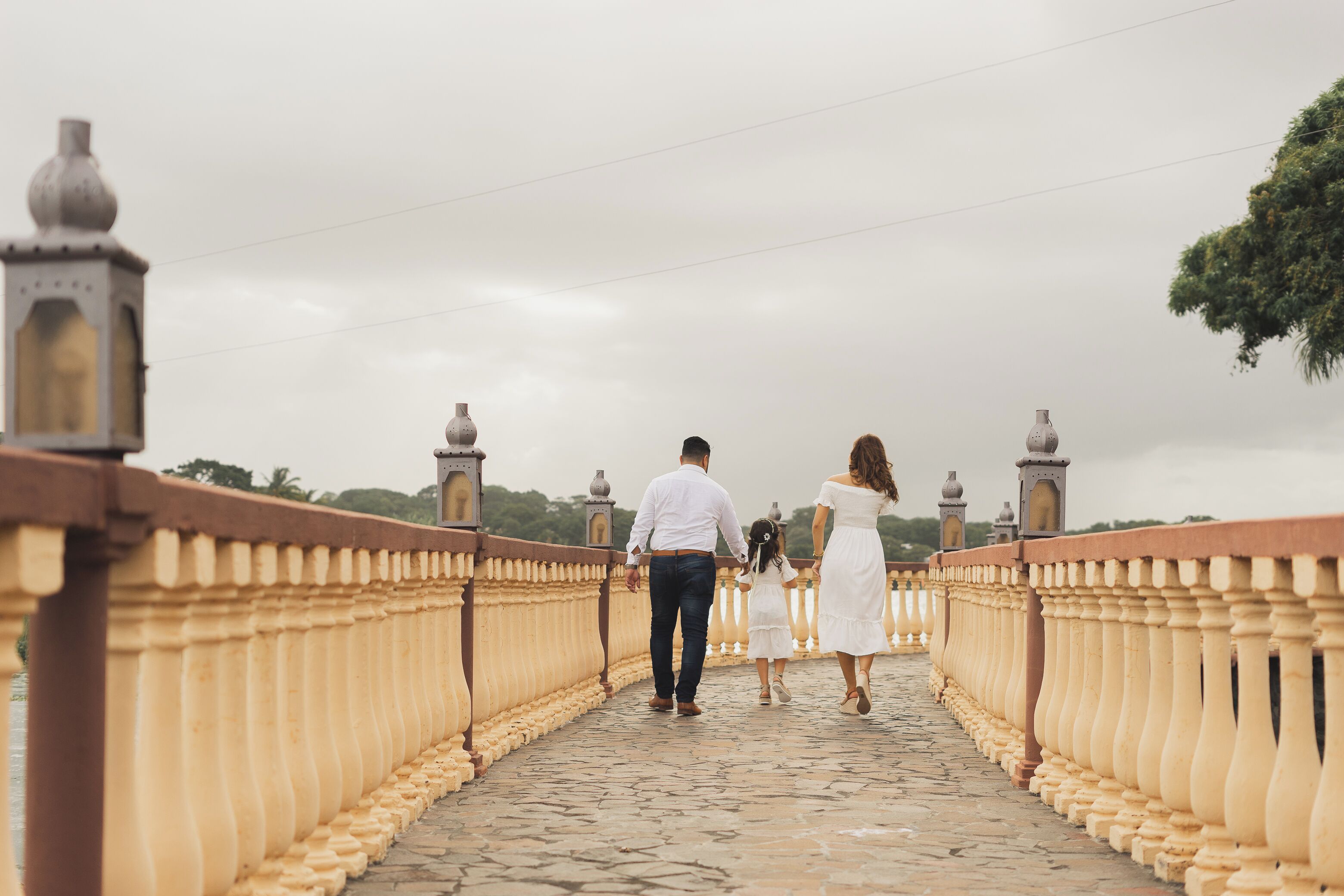 Uma ponte de pedra com grades ornamentadas e uma família caminhando sobre ela.