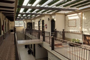 Área externa coberta com piso de pedra, corrimão de metal e plantas em vasos.