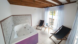 Quarto com uma banheira grande, duas poltronas, uma mesinha e varanda com vista.
