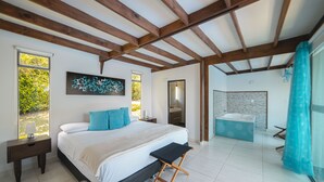 Quarto com cama grande, mesa de cabeceira, janela com vista, banheiro com banheira e vigas de madeira no teto.