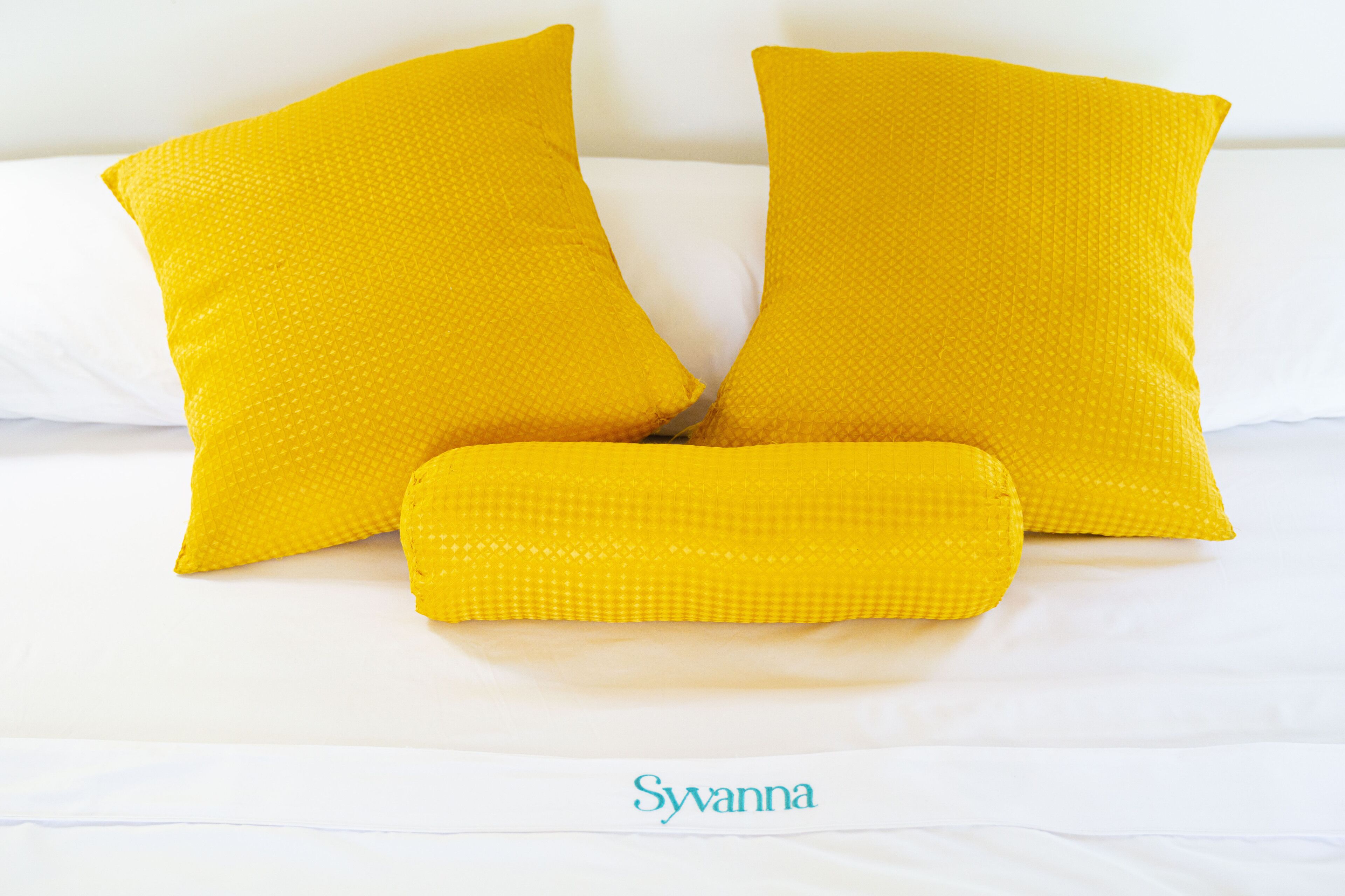 Uma cama com roupa de cama branca e três almofadas amarelas.