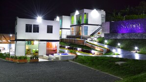 Um hotel moderno com uma entrada bem iluminada, uma escadaria visível e um jardim ajardinado.