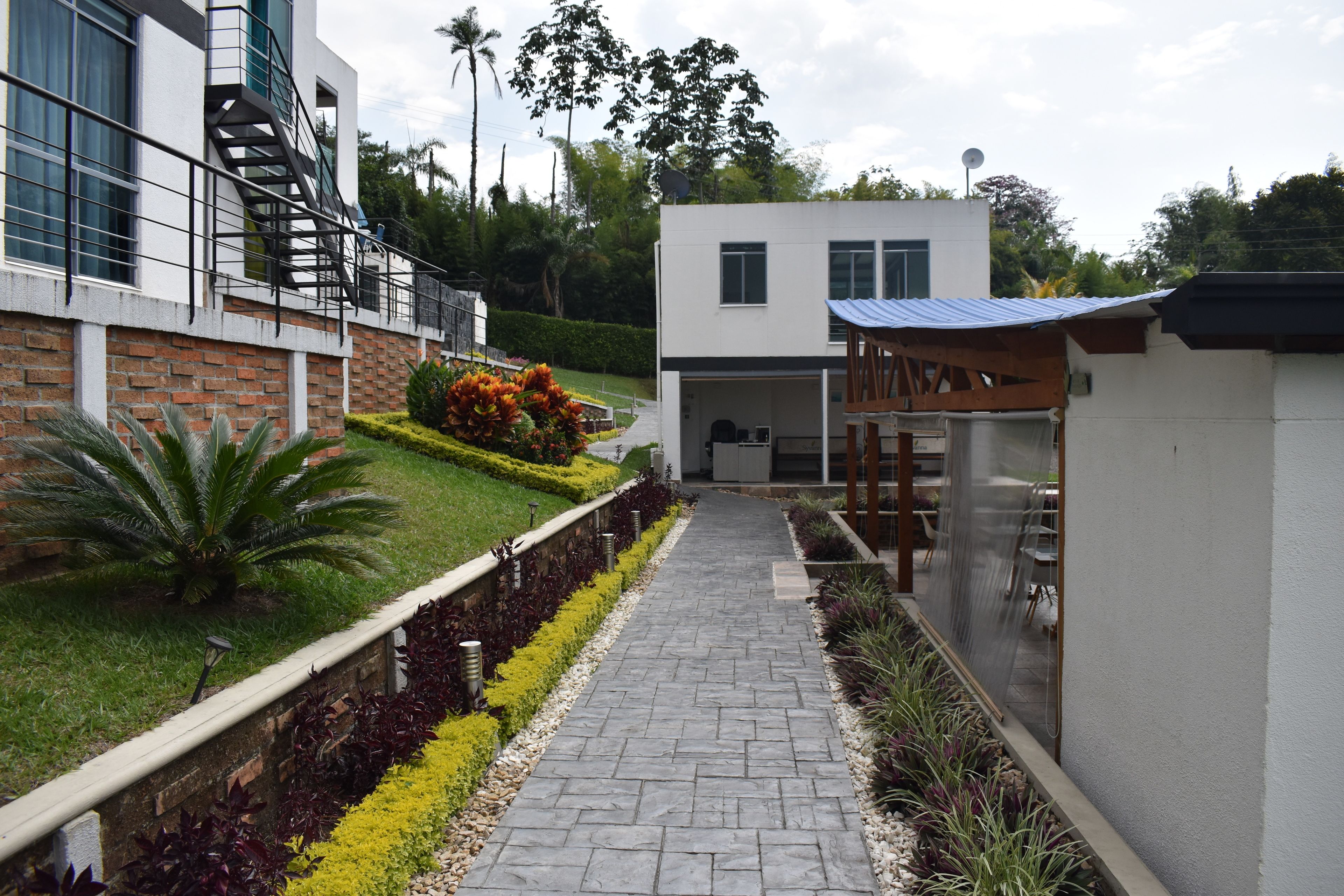 Um edifício moderno com fachada de tijolos, um caminho de pedra e um jardim bem cuidado com diversas plantas e flores.