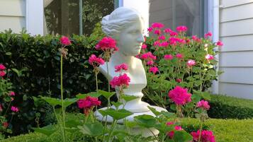 Jardim com busto branco cercado por flores cor-de-rosa.
