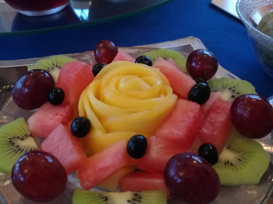 Uma travessa de frutas com melancia, kiwi, uvas e um mango no centro, sobre um prato de vidro.