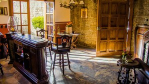 Quarto com parede de pedra, porta de madeira e um espaço bar com bancos e mesa.