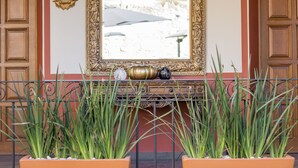 Um espelho decorativo com moldura dourada ornamentada, um pequeno relógio e vasos decorativos sobre uma lareira.