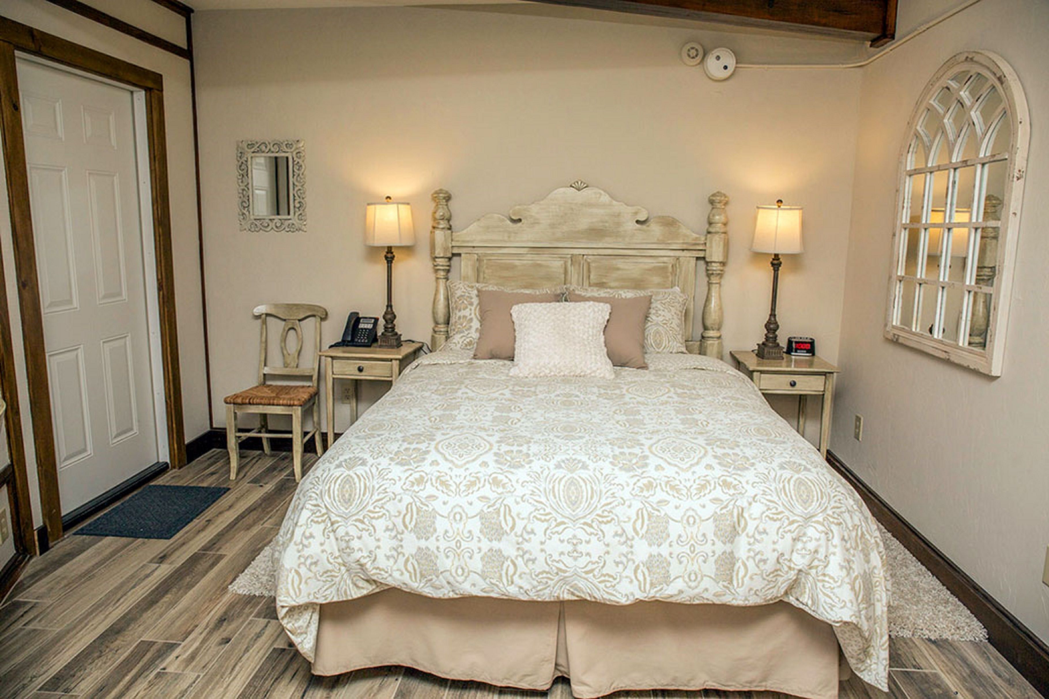 Quarto bem arrumado com uma cama grande, duas mesas de cabeceira com abajures, uma cadeira e um espelho na parede.