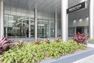 Entrada de hotel moderna com fachada de vidro, porta giratória e placa para apartamentos Meriton.