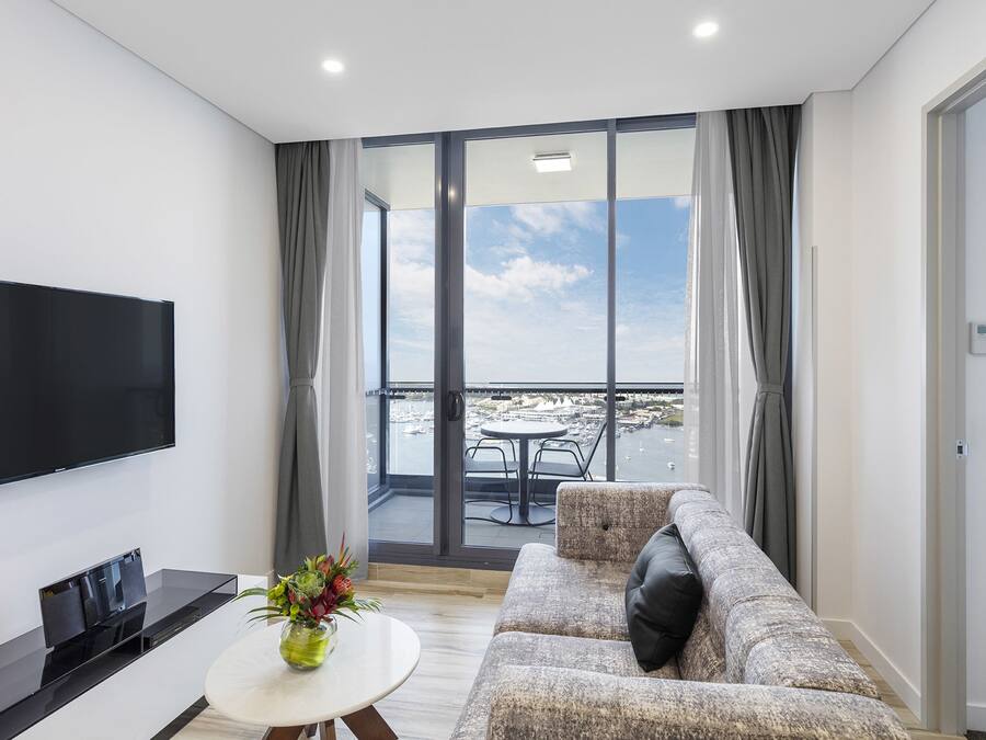 Uma sala de estar moderna com televisão de tela plana, sofá, mesa de centro com uma planta e varanda com vista para a cidade.