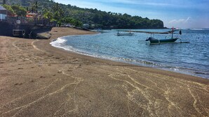 Uma praia com barcos, uma estrutura de madeira e uma colina arborizada.