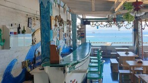 Um restaurante à beira-mar com um balcão comprido, mesas ao ar livre e vista para o oceano.