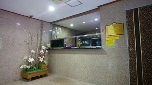 Uma área de recepção com balcão, arranjo de flores, placa na parede e câmera de segurança.