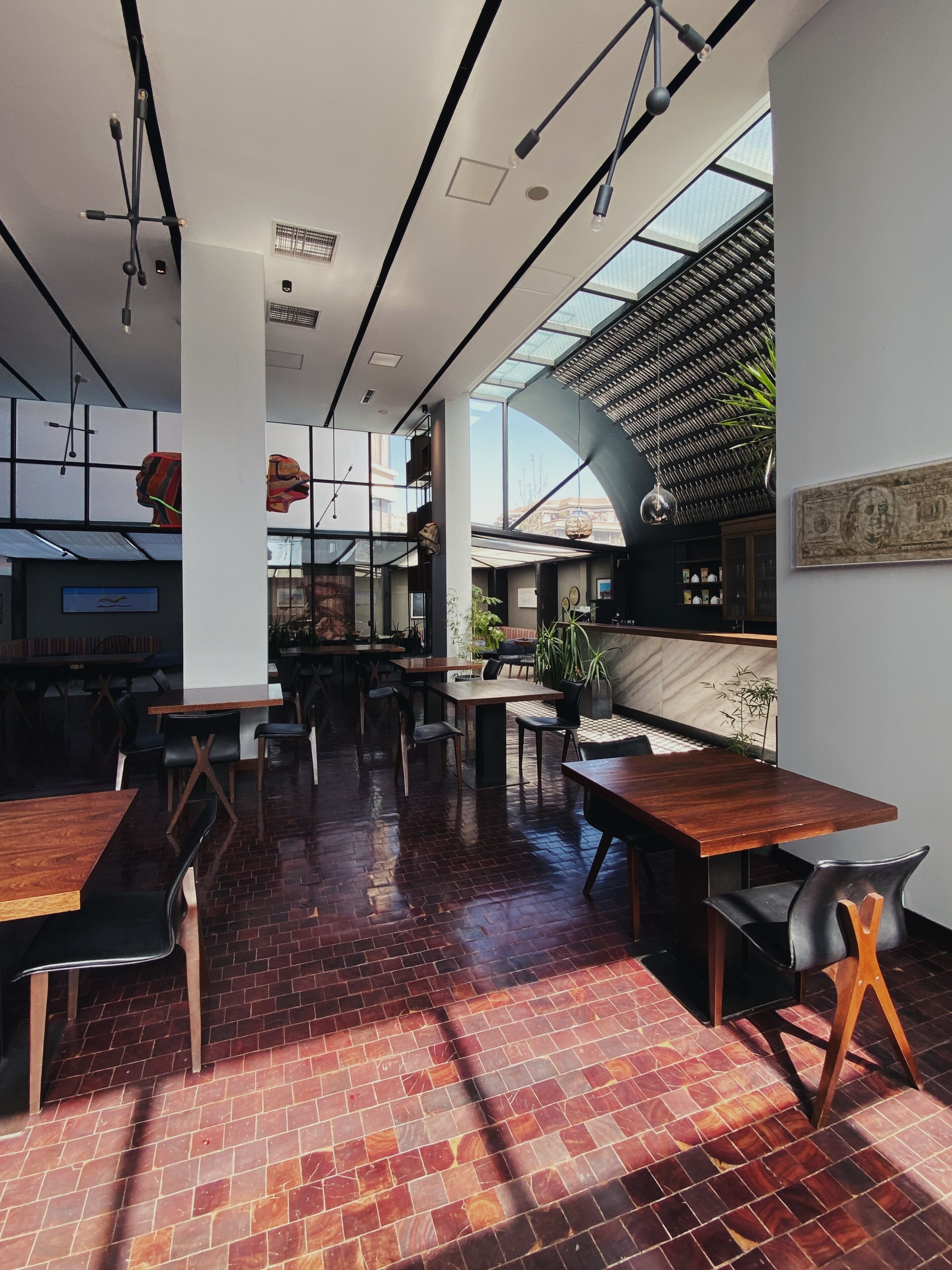 Um restaurante espaçoso com pé-direito alto, grandes janelas e uma combinação de mobiliário de madeira e metal.
