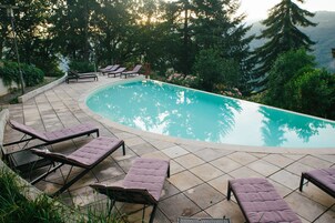 Piscina com espreguiçadeiras e vista para árvores e colinas.