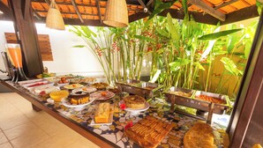 Buffet com diversos alimentos e um cenário com plantas tropicais.