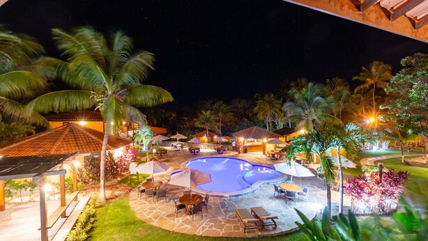 Uma área de piscina à noite, com piscina circular, cadeiras de descanso e guarda-sóis.