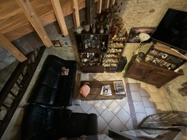 Uma sala de estar aconchegante com um sofá de couro preto, uma mesa de centro de madeira e diversos objetos decorativos, incluindo uma estante com cerâmica e uma televisão.