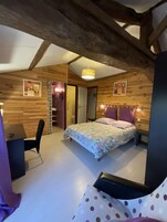 Quarto com paredes de madeira, cama com roupa de cama florida, escrivaninha e uma cadeira.