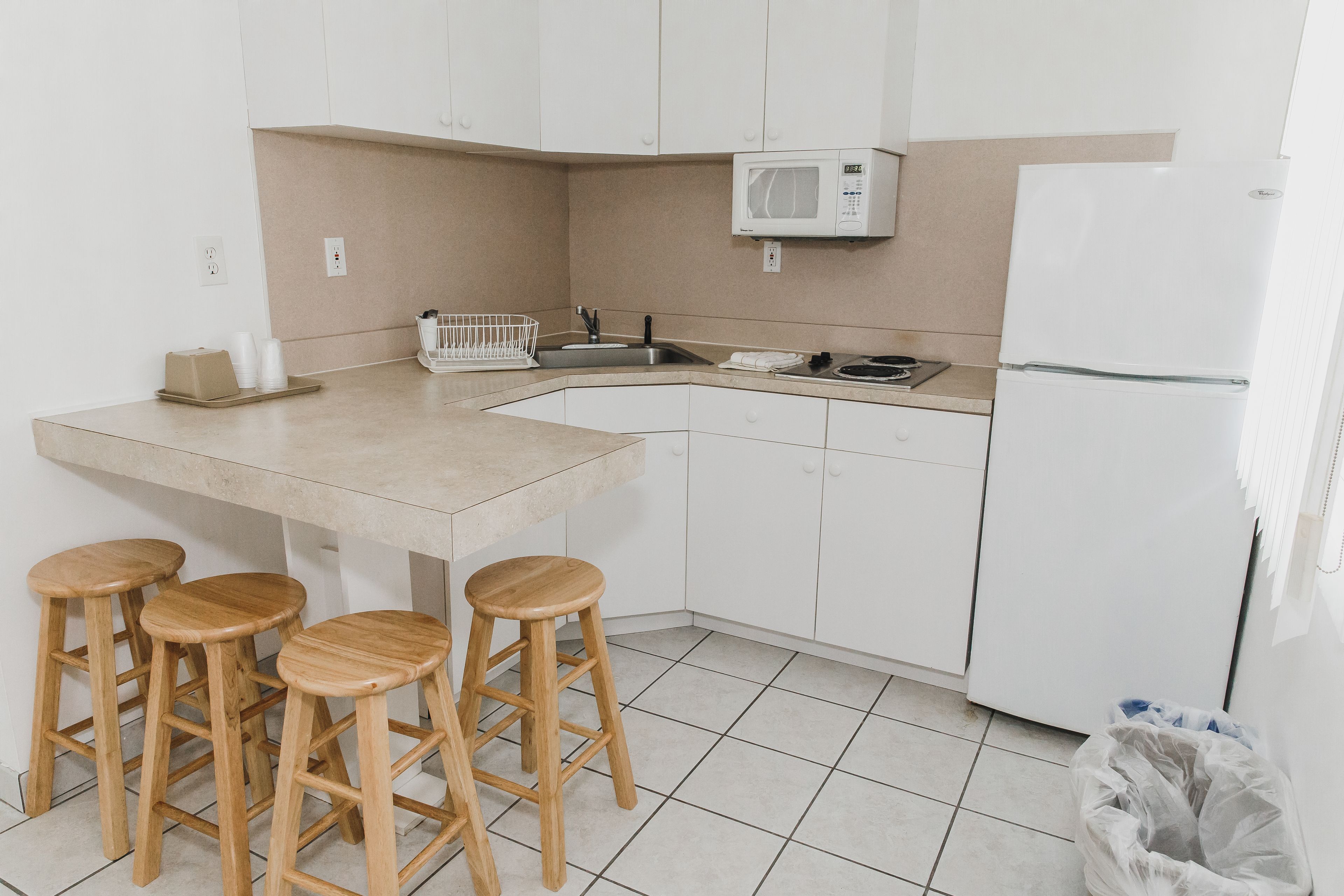 Cozinha compacta com micro-ondas, geladeira e pia. Três banquetas de madeira ao redor da ilha.