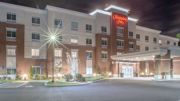 Um hotel Hampton Inn com fachada de tijolos modernos, várias janelas e uma entrada bem iluminada.