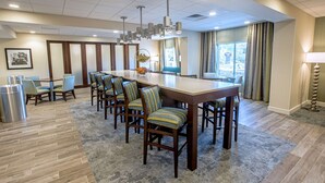 Uma sala de jantar de hotel com uma mesa comprida, cadeiras listradas e um candelabro.