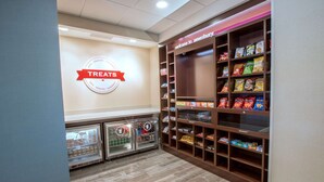 Espaço para lanches com um letreiro 'Treats', expositores refrigerados e prateleiras cheias de diversos petiscos.