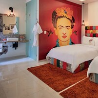 Um quarto com uma cama grande, um banheiro com pia e espelho, e um mural vibrante na parede.
