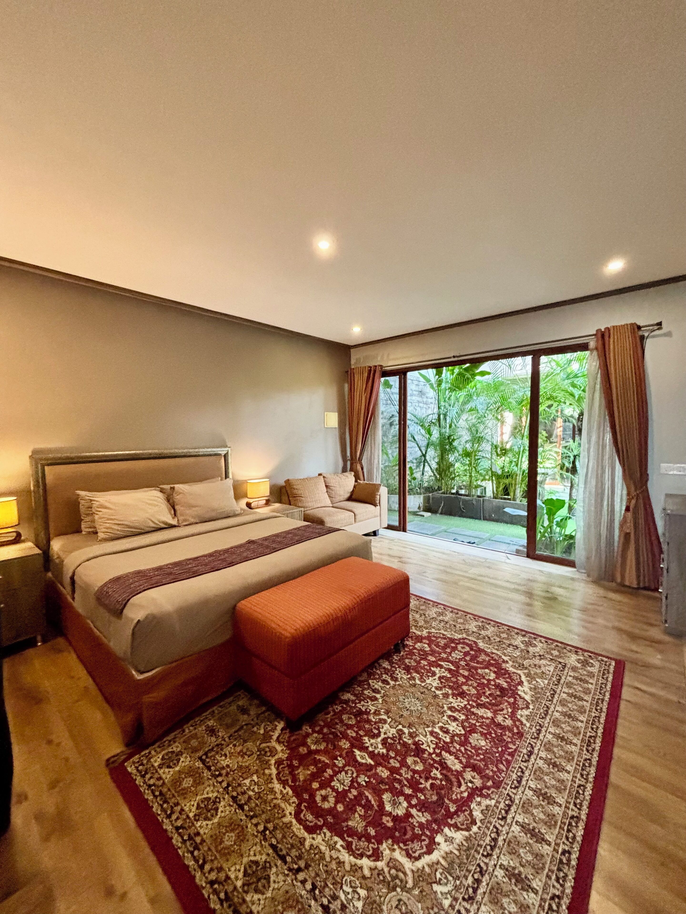 Quarto com uma cama grande, um espaço para sentar e vista para um jardim através de uma porta de vidro deslizante.