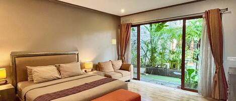 Quarto com uma cama grande, um espaço para sentar e vista para um jardim através de uma porta de vidro deslizante.