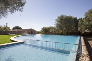 Piscina com borda curva, rodeada por um muro de pedra e área gramada.