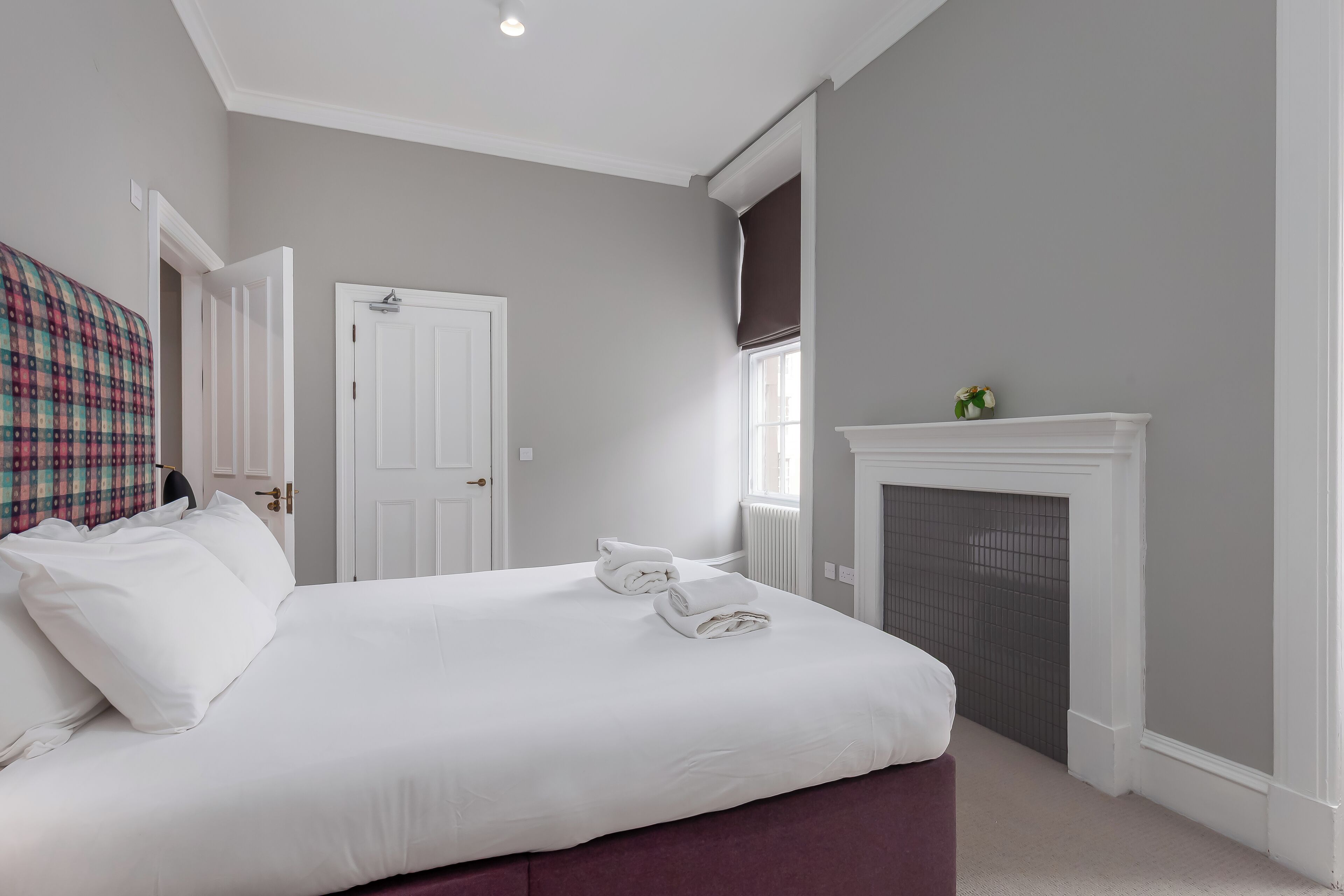 Quarto com cama grande, porta branca, lareira e janela.