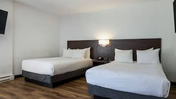 Quarto de hotel com duas camas, uma mesa de cabeceira e uma luminária na parede.