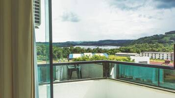 Uma varanda com guarda-corpo de vidro, com vista para uma paisagem com colinas e um corpo de água.