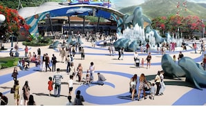 Área externa movimentada com um grande letreiro para Ocean Park, apresentando uma escultura de golfinho e fontes de água.