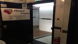 Entrada de hotel com placa indicando Hotel Vênus, incluindo informações de contato e detalhes de localização.