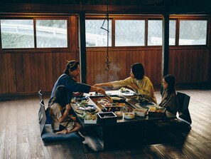 Disposição tradicional de refeição japonesa com mesa de madeira, tatames e vista para uma paisagem nevada através de grandes janelas.