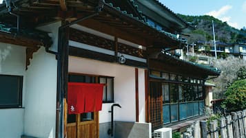 Uma casa japonesa tradicional com fachada de madeira, entrada coberta por telhas e uma toalha vermelha pendurada na porta.