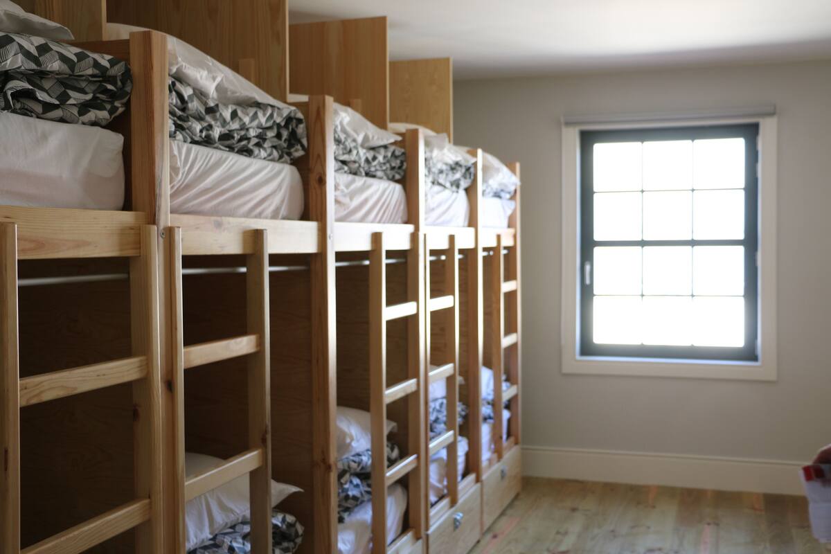 Quarto com beliches, janela e piso de madeira.