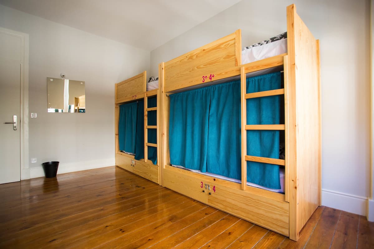 Quarto com beliches de madeira, um espelho na parede e um cesto de lixo preto.