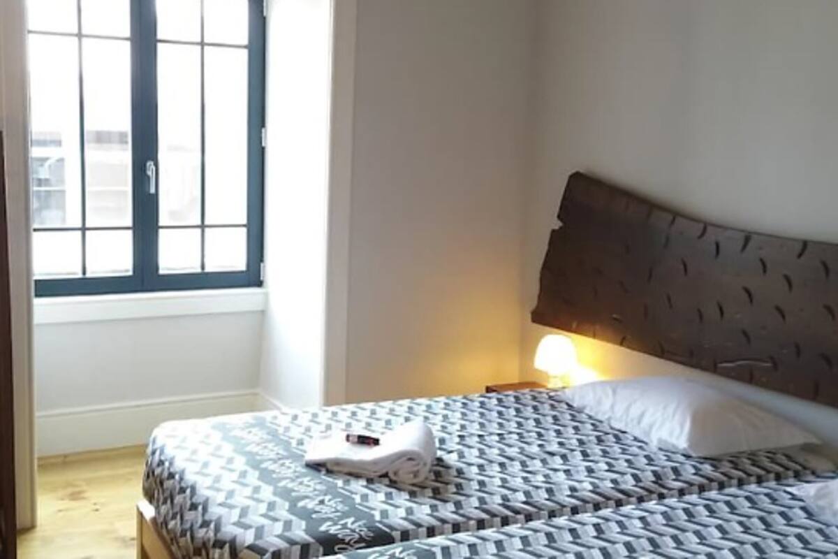 Quarto de hotel com cama, janela, cabideiro fixado na parede e abajur.