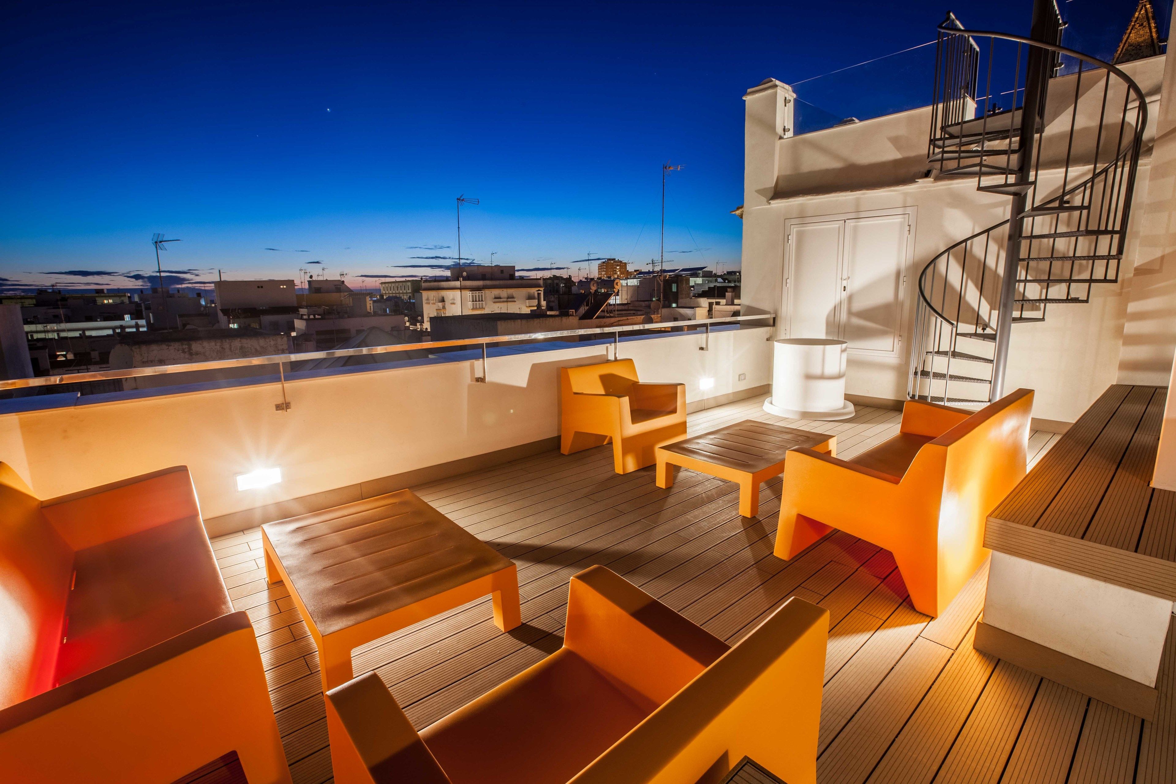 Terraço no telhado com piso de madeira, assentos laranja e uma escada em espiral.