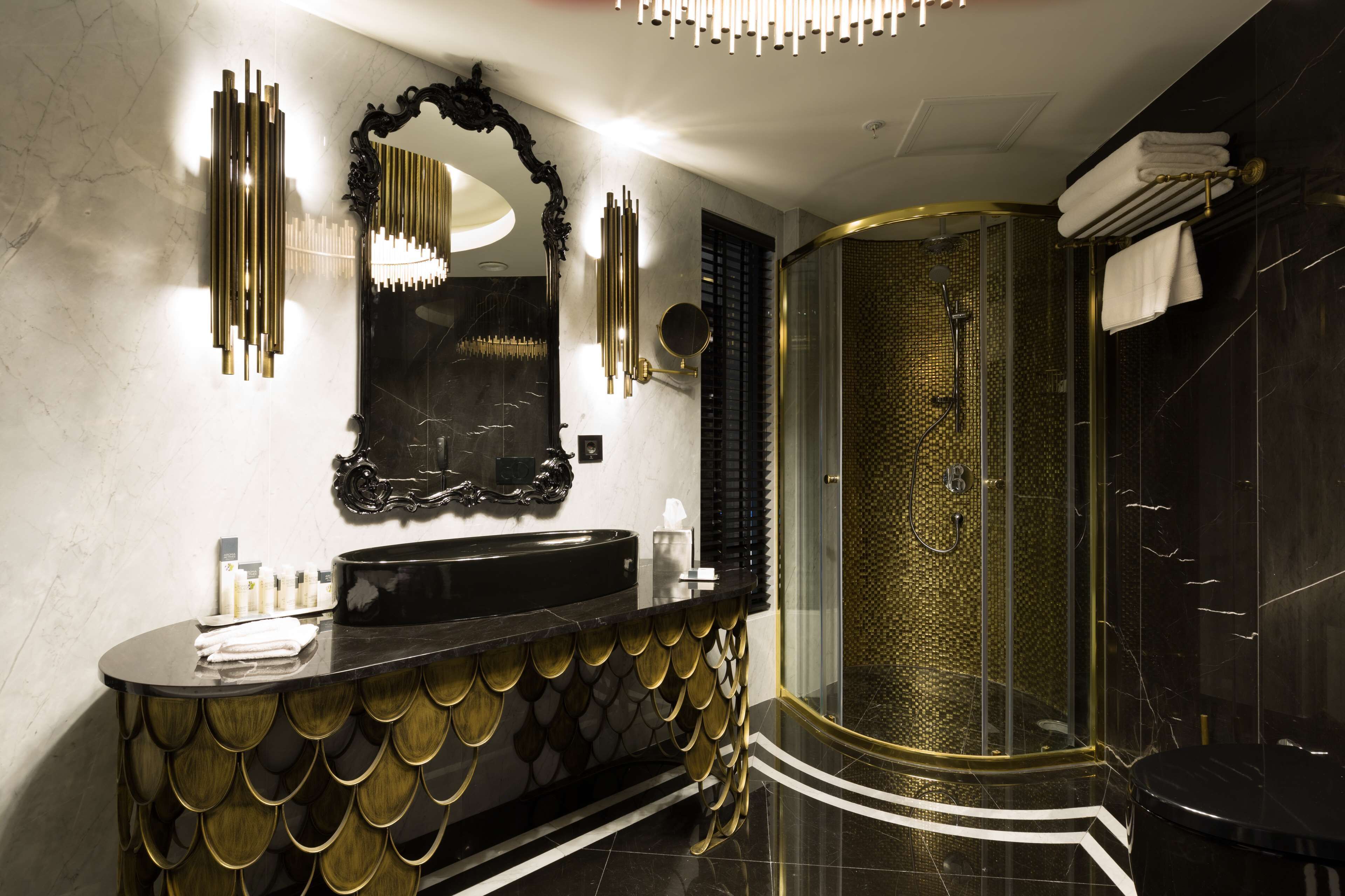 Um banheiro luxuoso com pia preta, detalhes dourados, um espelho grande e box de vidro.