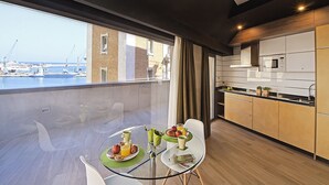 Cozinha moderna com vista para o porto, área de refeições com itens de café da manhã e varanda com mesa de vidro.
