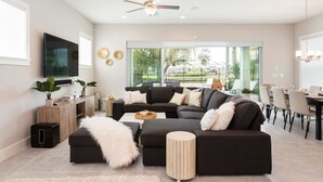 Uma sala de estar moderna com um sofá seccional, uma TV de tela plana e uma área de jantar com mesa e cadeiras.
