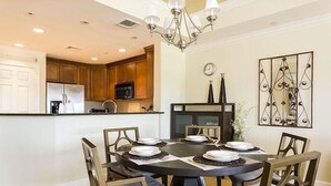 Uma sala de jantar com uma mesa redonda posta para seis pessoas, rodeada por cadeiras de madeira com assentos acolchoados.