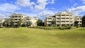 Um hotel com vários andares, teto plano, diversas varandas e um jardim bem cuidado na frente.