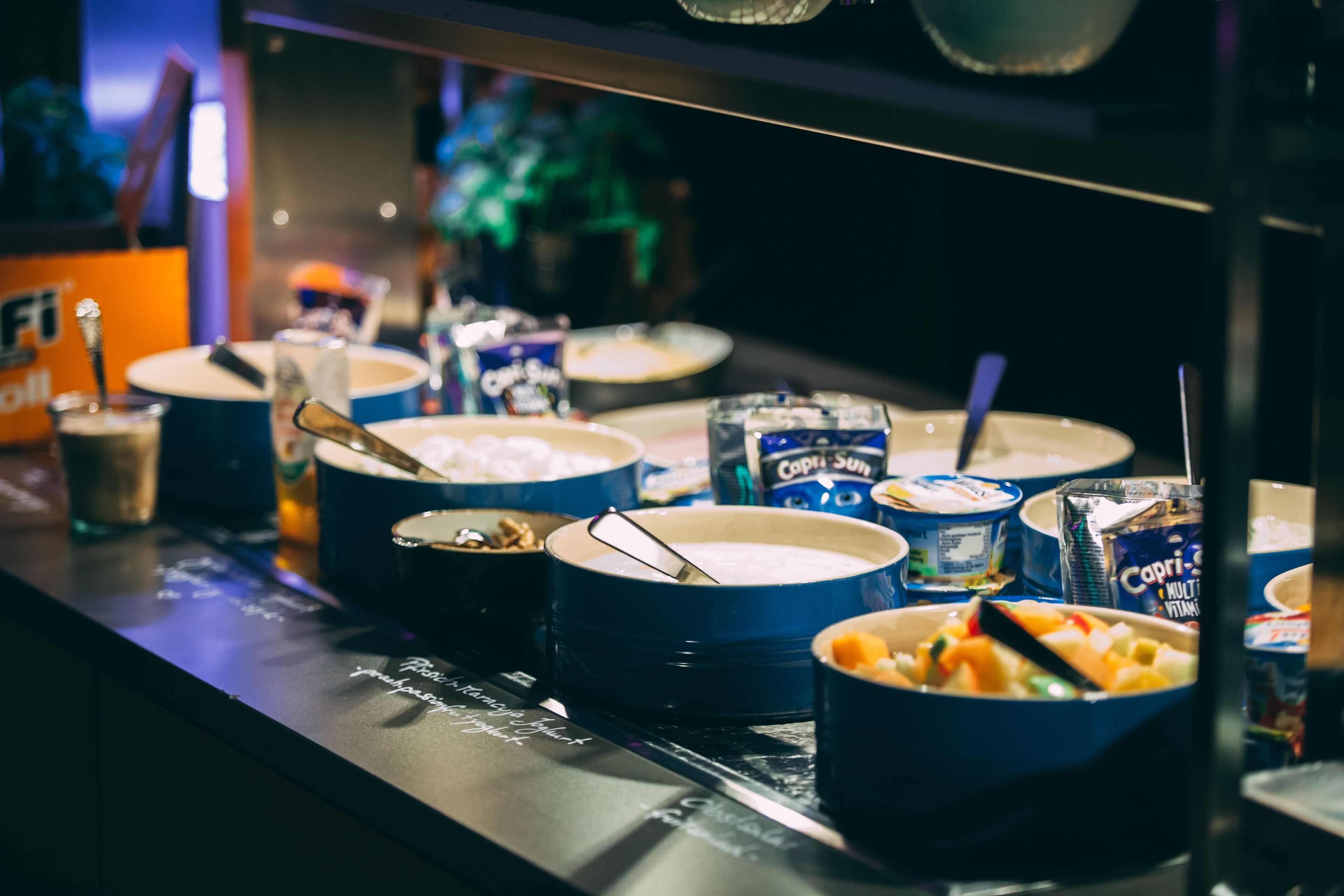 Buffet com diversos alimentos e bebidas, incluindo sopas em tigelas e iogurtes em recipientes.