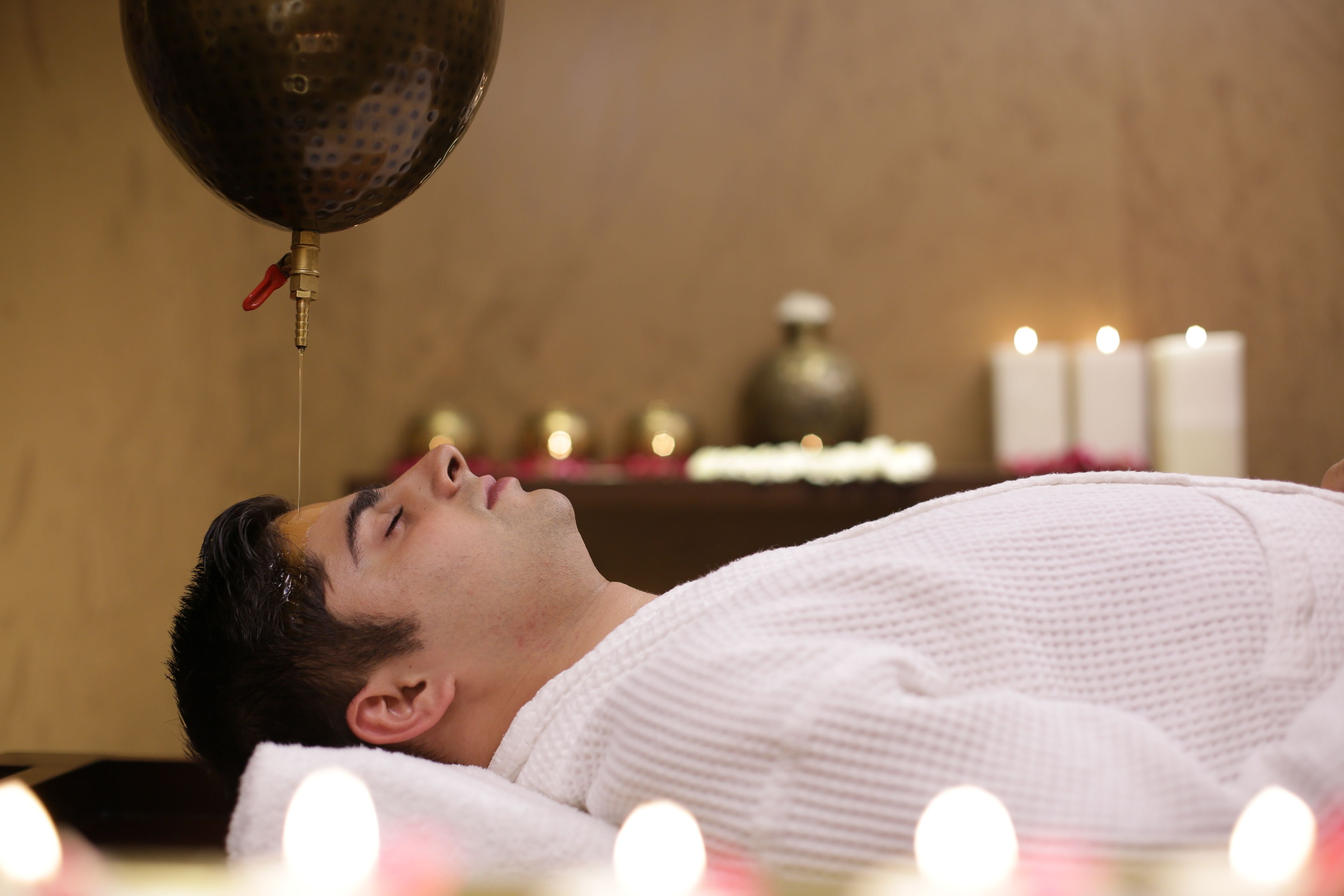 Uma pessoa deitada em um quarto com velas e uma cadeira de massagem.