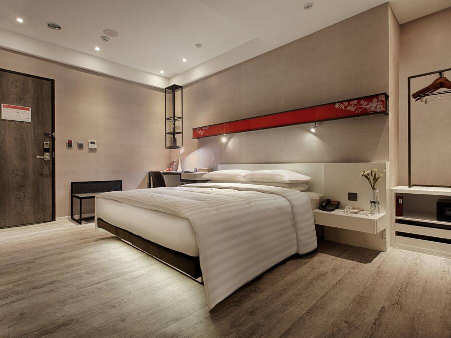 Quarto de hotel moderno com uma cama grande, mesas de cabeceira, escrivaninha e guarda-roupa.